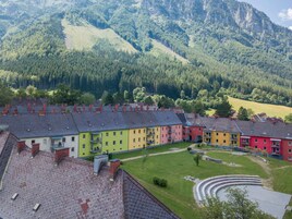 Um bairro residencial com casas coloridas, um pátio central e montanhas ao fundo.