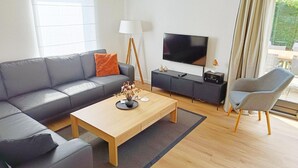 Uma sala de estar moderna com um sofá cinza, uma mesa de centro de madeira, uma poltrona cinza, uma televisão e um pequeno armário.