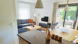 Uma sala de estar moderna com sofá, mesa de centro, televisão e área de jantar com mesa e cadeiras.