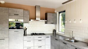 Cozinha moderna com fogão a gás, pia de aço inoxidável e painel de azulejos brancos.