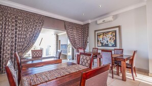 Uma área de refeições com mesa e cadeiras de madeira, cortinas estampadas e um quadro na parede.