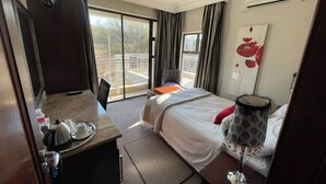 Quarto de hotel com cama, escrivaninha, cadeira, janela com cortinas e vista para o exterior.