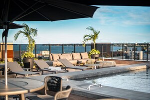 Uma área de piscina no terraço com cadeiras de descanso, uma mesa pequena e um grande guarda-sol.