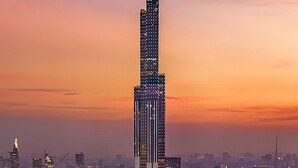 Um edifício alto com design vertical marcante, rodeado por outros edifícios imponentes na paisagem urbana.