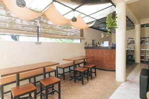 Um café com mesas e cadeiras de madeira, um balcão com cardápio e uma planta pendente.