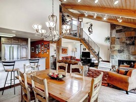 Uma sala de estar ampla com uma mesa de jantar de madeira, uma escada que leva a um andar superior e uma lareira de pedra.