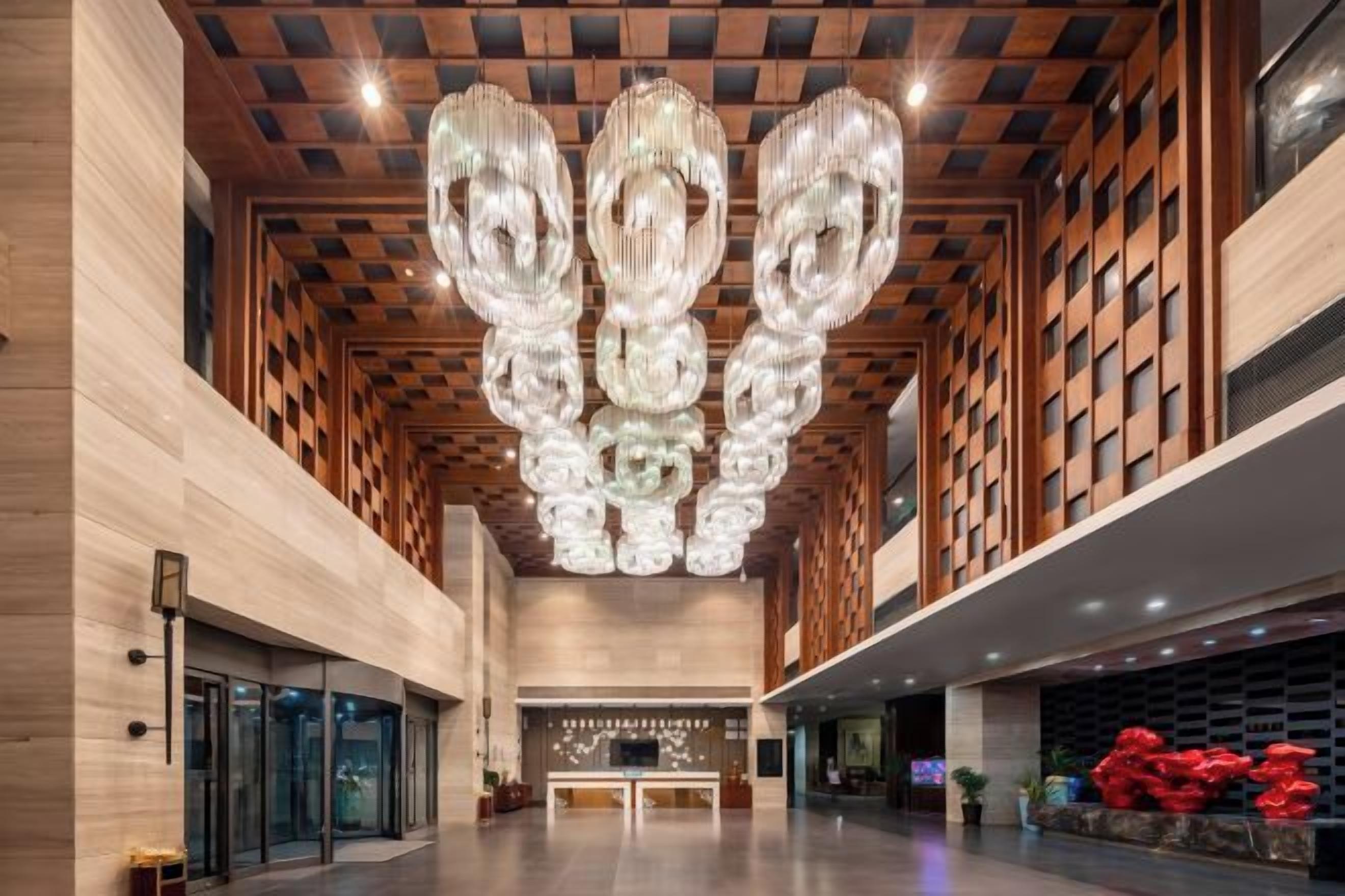 Um hall amplo com um lustre moderno, painéis de madeira e um balcão de recepção.