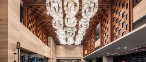 Um hall amplo com um lustre moderno, painéis de madeira e um balcão de recepção.