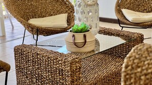 Cadeiras de vime com almofadas, uma mesa com tampo de vidro, um cesto trançado e um vaso com planta.