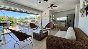 Sala de estar moderna com móveis de vime, vista para piscina e área de cozinha.
