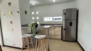 Uma cozinha moderna com geladeira de aço inoxidável, uma ilha pequena com banquetas e uma janela sobre a pia.