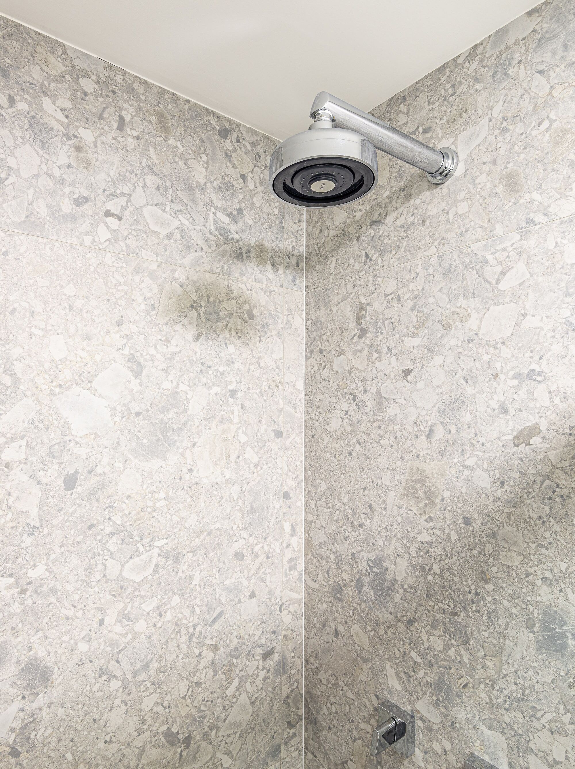 Chuveiro com design moderno, apresentando um chuveiro em arco e parede com padrão de azulejos pontilhados.