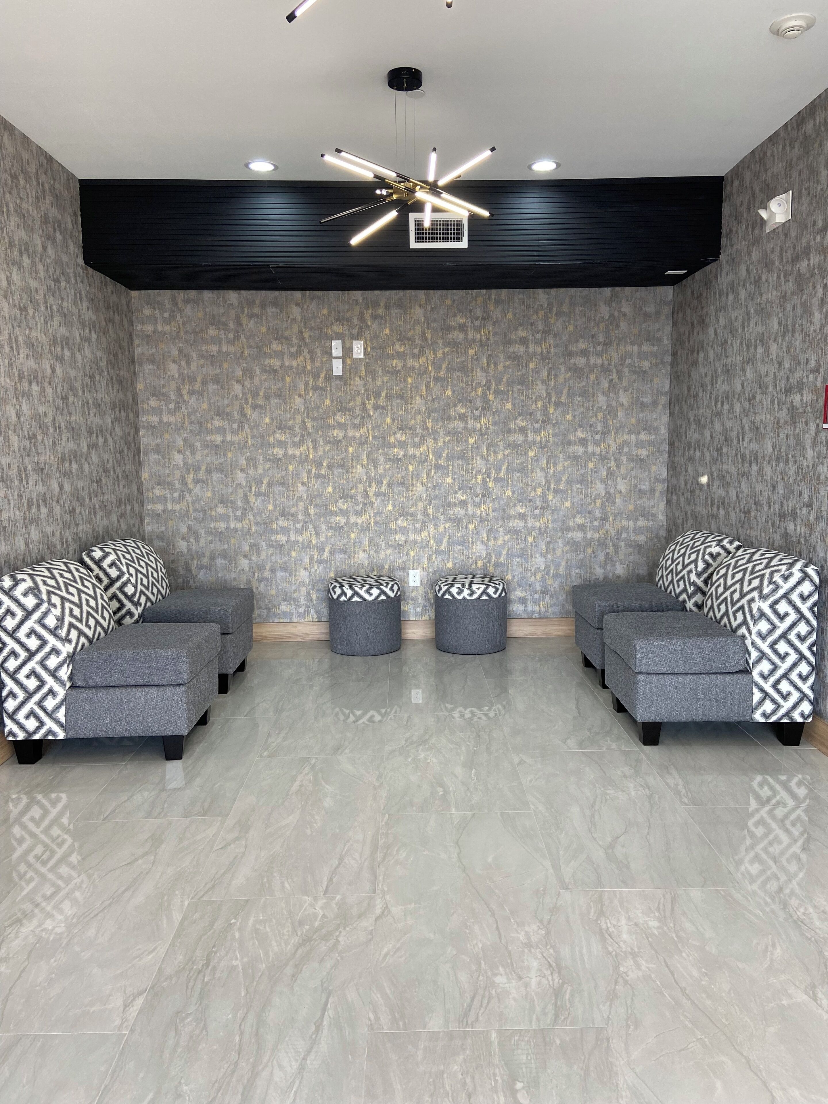 Quarto moderno com sofás e pufes cinzas, parede estampada e ventilador de teto.