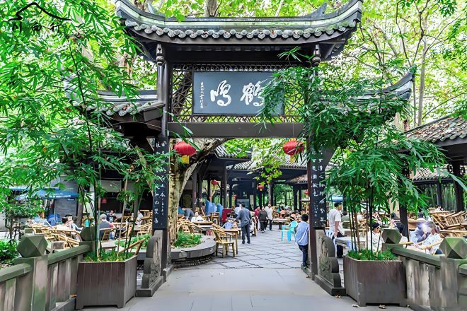 Um pavilhão tradicional chinês com uma placa, rodeado por bambus e áreas de estar ao ar livre.