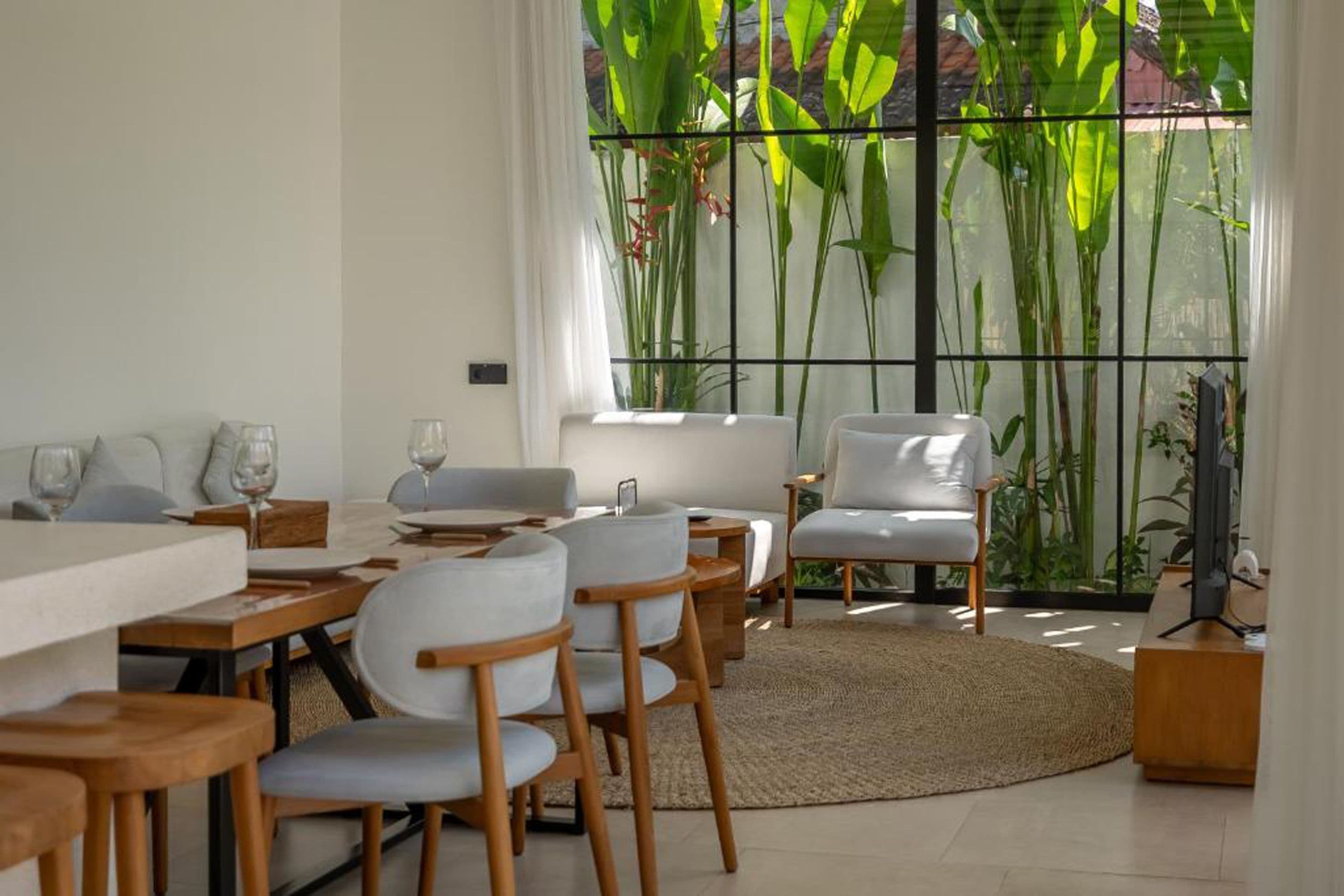 Uma área de refeições com uma grande janela, cadeiras de madeira e uma mesa com decoração moderna.