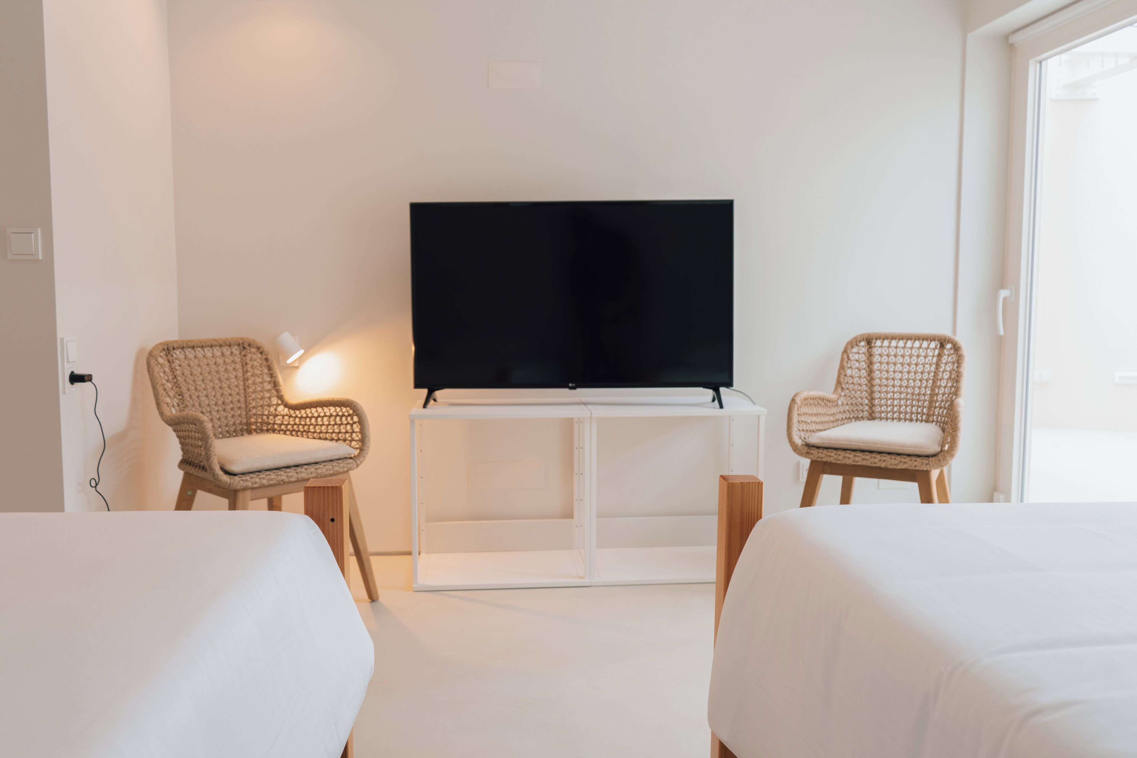 Quarto de hotel com televisão de tela plana, duas cadeiras de vime e uma cama.