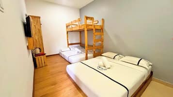 Quarto pequeno e compacto com beliche, uma cama de solteiro, um armário de madeira e uma televisão.
