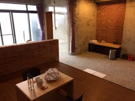 Quarto com mesa de madeira, cadeiras, um banco, lixeira e janela com cortinas.