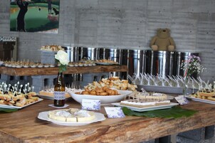 Mesa de buffet com diversos alimentos e um urso de pelúcia em uma prateleira.