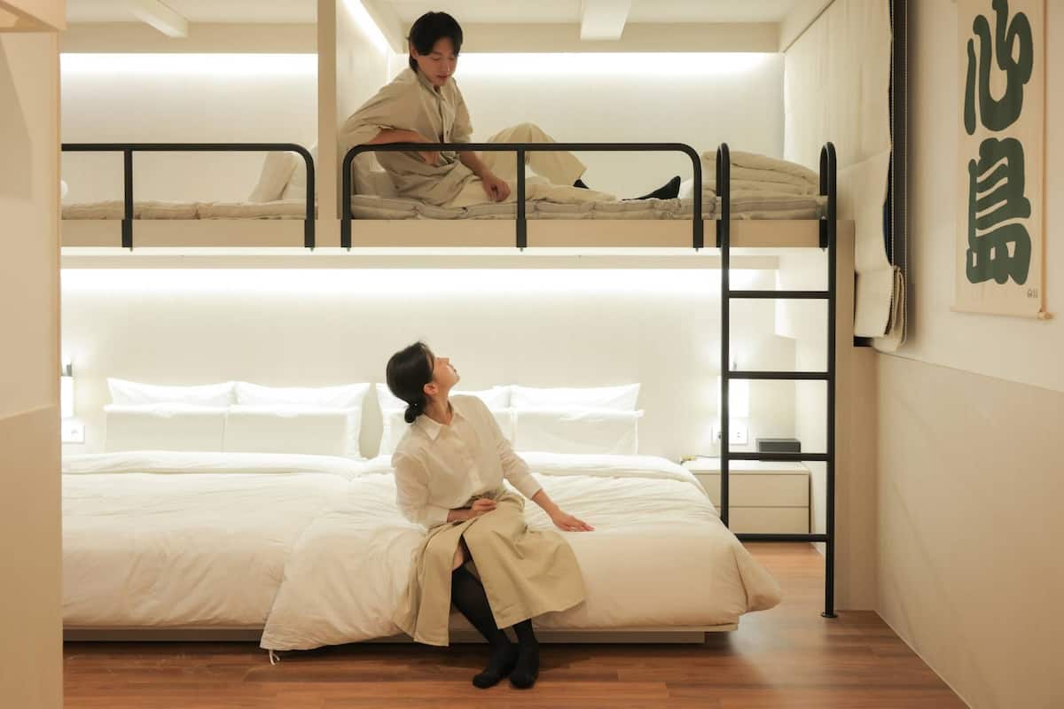 Quarto com beliche, com uma pessoa sentada na cama inferior e outra deitada no belo superior.