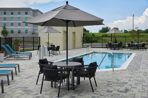 Uma área de piscina externa com espreguiçadeiras, uma mesa com cadeiras e guarda-sóis.
