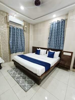 Quarto bem arrumado com uma cama grande, mesa de cabeceira, ar condicionado e cortinas estampadas.