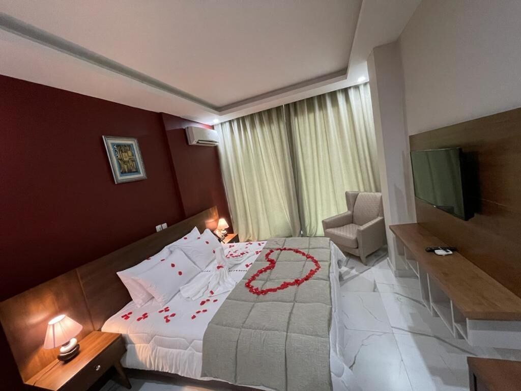 Quarto de hotel com cama, escrivaninha, cadeira, televisão e cortina.