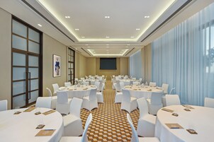 Uma sala de conferências com várias mesas redondas, cadeiras brancas e um padrão de piso xadrez.