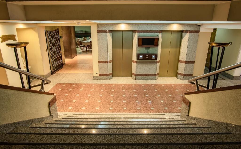 Um saguão de hotel com escadas revestidas de carpete, um balcão de recepção e uma tela de televisão.
