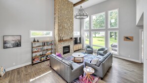 Uma sala de estar espaçosa com lareira de pedra, janelas amplas e móveis modernos.