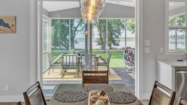 Uma sala de jantar com uma mesa posta para quatro pessoas, um lustre pendurado e vista para um pátio com mobiliário externo.