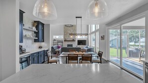 Uma cozinha espaçosa com uma ilha grande de mármore, armários azul-escuros e iluminação pendente.