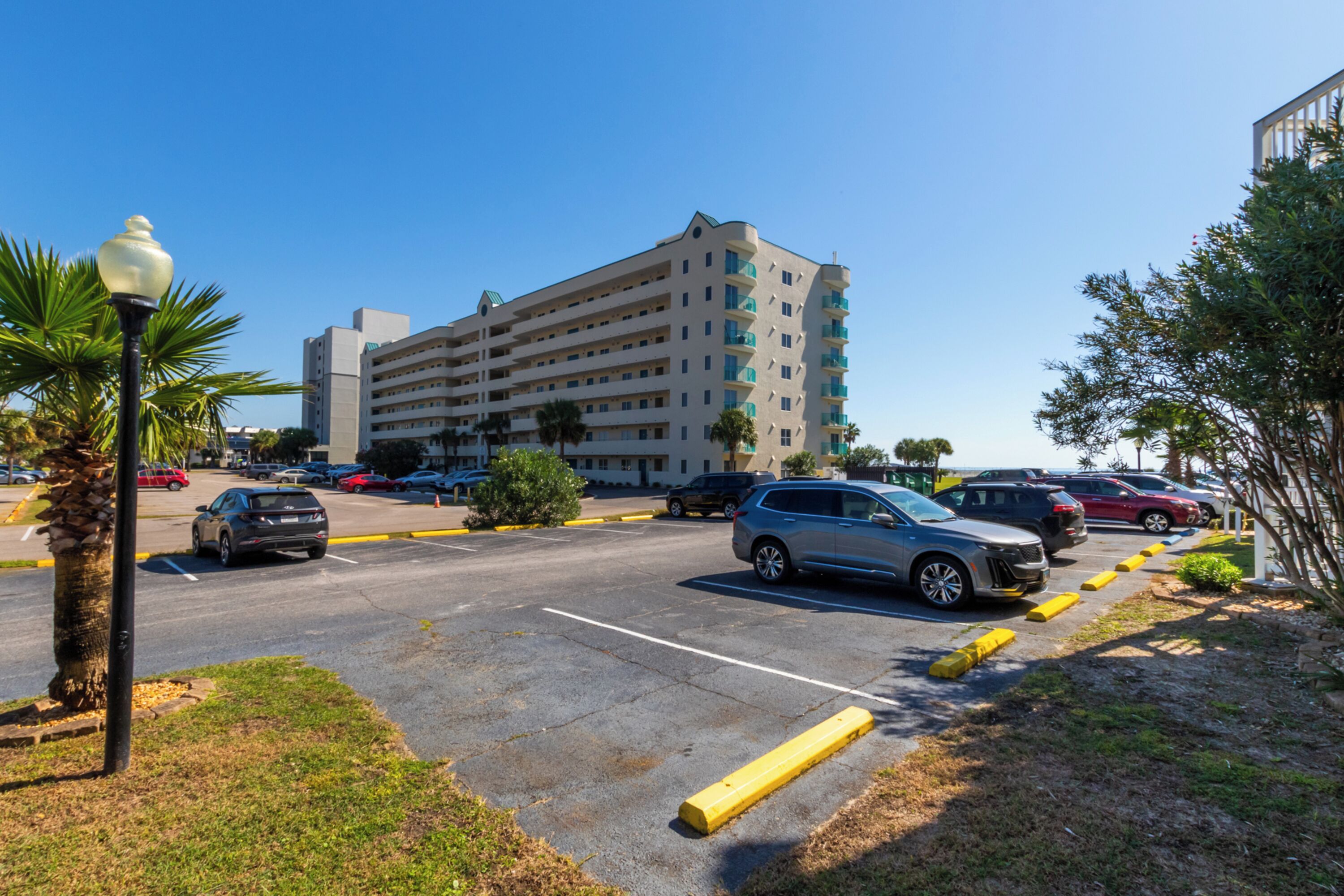 Um hotel de vários andares com design moderno, um estacionamento com vários carros e um céu azul e límpido.