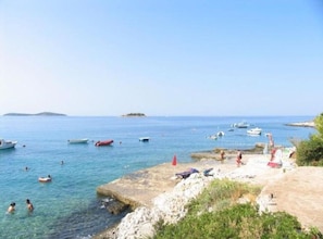 Cena de praia costeira com águas cristalinas, barcos e pessoas a nadar.
