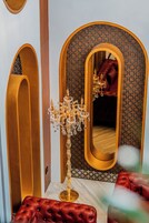 Quarto luxuoso com um espelho grande, um candelabro e um banco de couro vermelho.