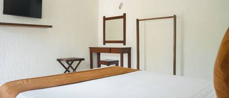 Quarto de hotel com cama, escrivaninha, cadeira, mesinha, espelho e televisão na parede.