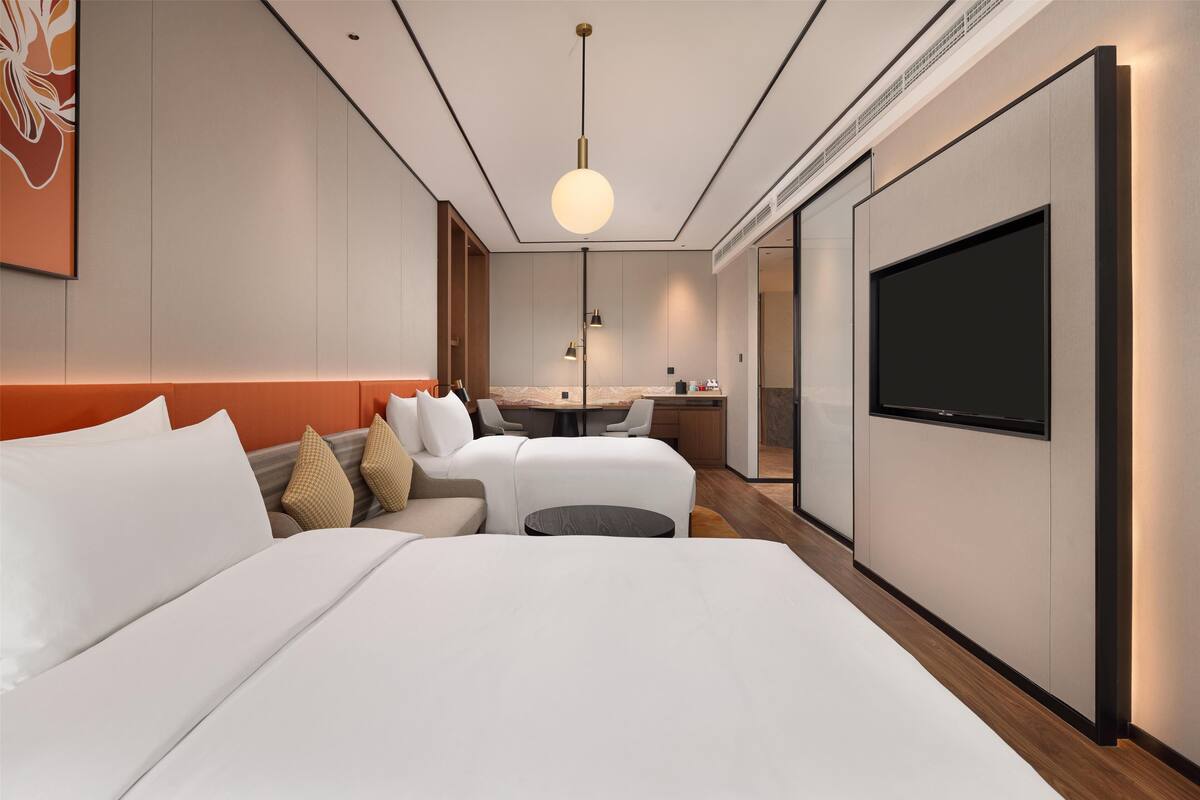 Quarto de hotel moderno com uma cama grande, um sofá, uma mesa de jantar e uma televisão.