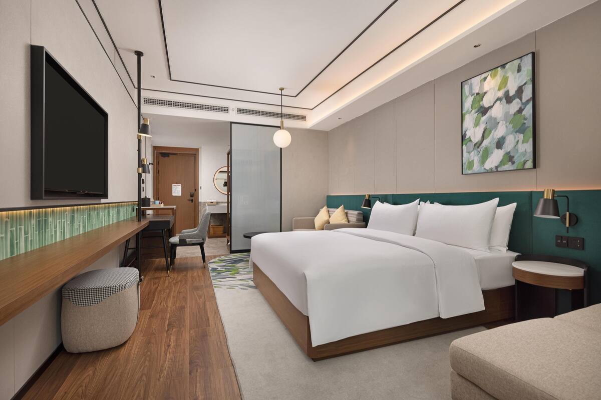 Quarto de hotel moderno com uma cama grande, uma escrivaninha, uma televisão e uma parede verde decorativa.