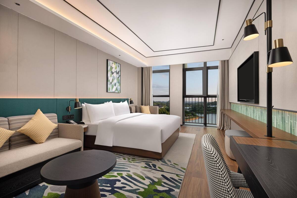 Quarto de hotel moderno com uma cama grande, um sofá, uma mesa de jantar e uma televisão.