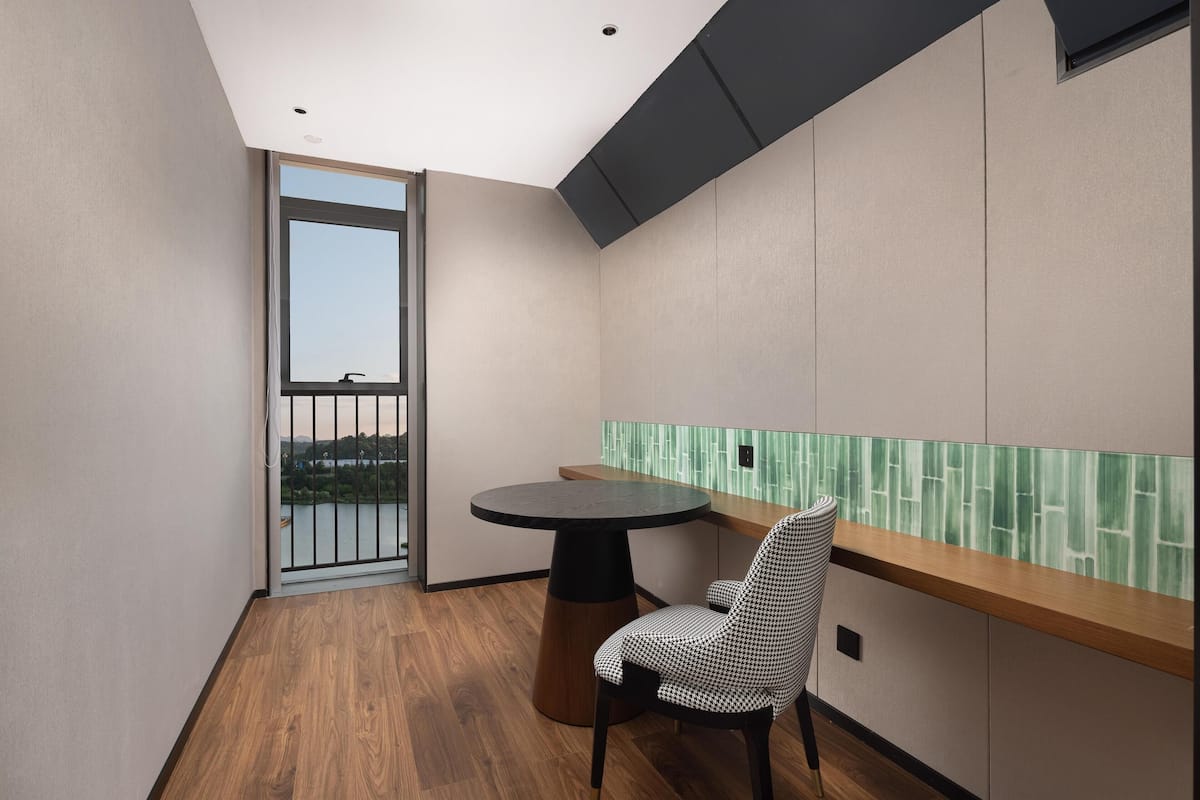 Uma pequena área de refeições com uma mesa redonda, uma cadeira xadrez e vista para um lago através de uma porta de correr.