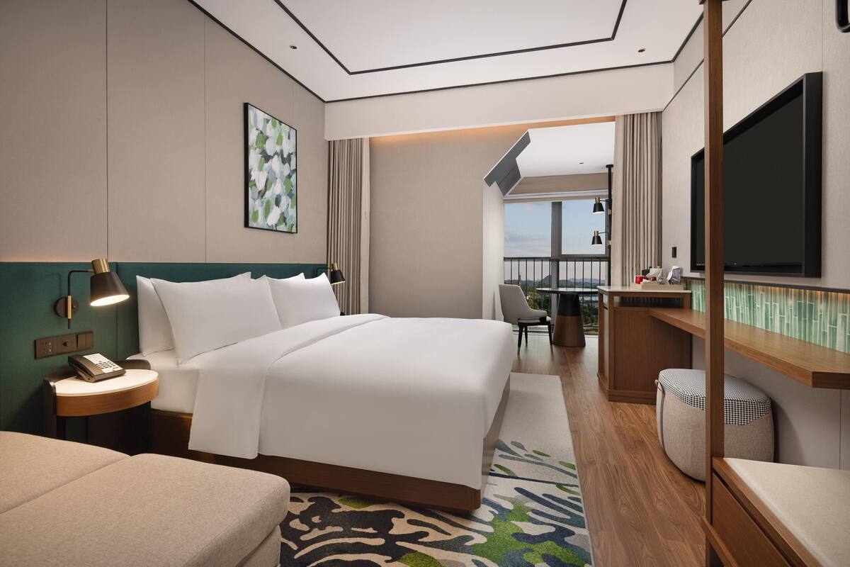 Quarto de hotel moderno com uma cama grande, mesas de cabeceira, escrivaninha e televisão.