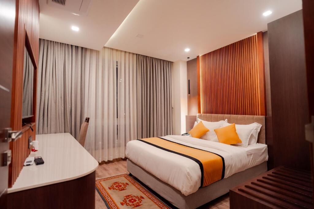 Quarto de hotel com cama, escrivaninha e janela com cortinas.
