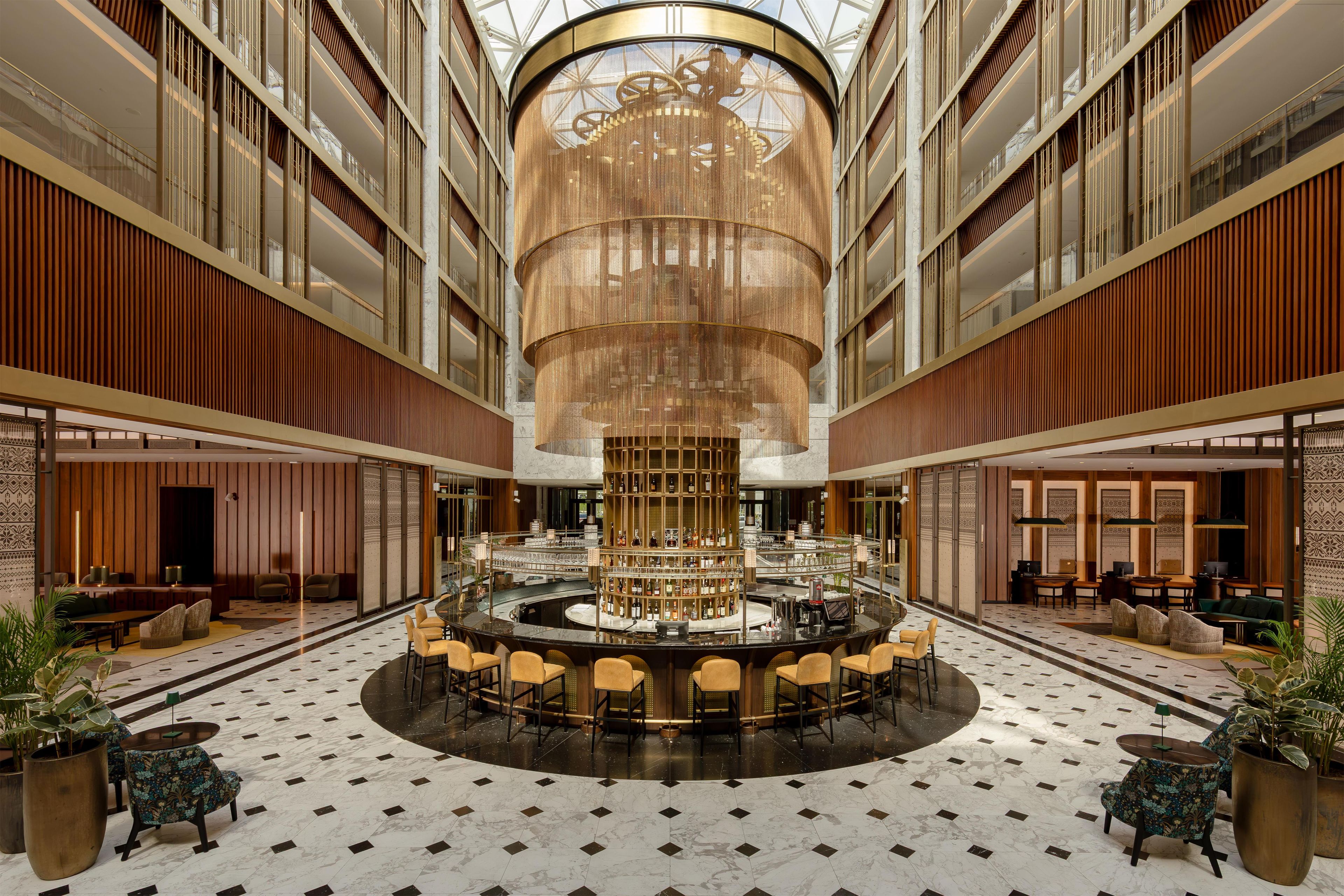 Um amplo saguão de hotel com bar central, pé direito alto e design moderno.