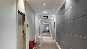 Um corredor longo e estreito com piso de carpete, paredes cinzentas e um objeto vermelho à esquerda.