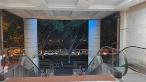 Um saguão de hotel com uma escadaria central, uma grande janela com vista para a rua e um chão de azulejos.