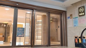 Entrada de hotel com design moderno, destacando uma grande porta de vidro e um letreiro com o logotipo 'H'.