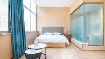 Quarto de hotel com cama, mesa redonda pequena, mesa de cabeceira, janela com cortinas e porta de vidro.
