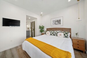 Quarto moderno com uma cama grande, uma televisão de tela plana na parede e um quadro emoldurado acima da cama.