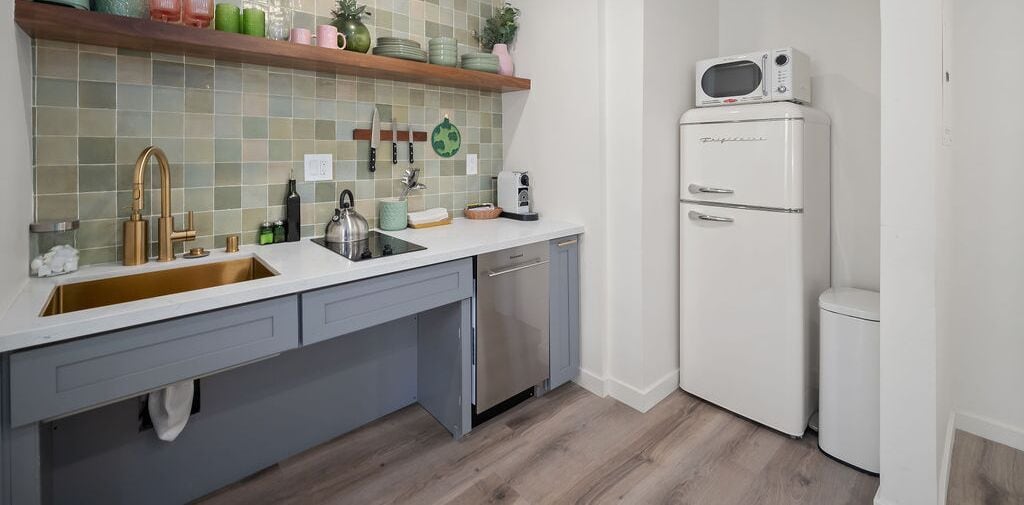Uma cozinha equipada com pia, chaleira, micro-ondas e geladeira.