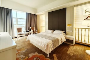 Quarto de hotel com cama, escrivaninha, cadeira, janela com cortinas e varanda.